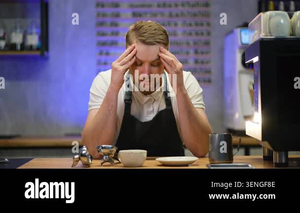 Young male barista sitting at the counter feeling stressed and tired ...