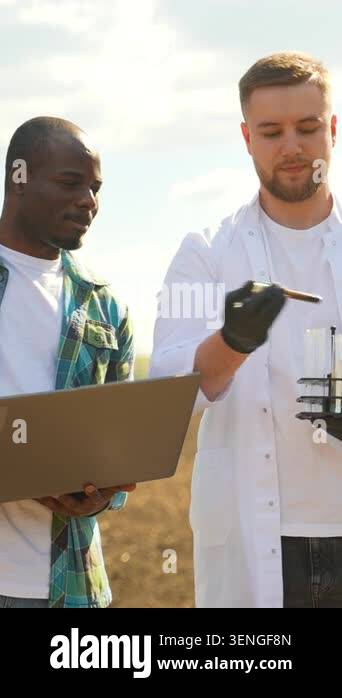 Scientist showing a soil sample in a test tube to a farmer holding a ...