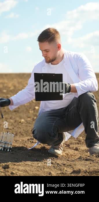 Male agronomist in a white coat and gloves taking soil samples for ...