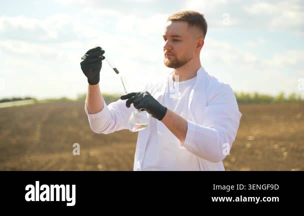 Professional laboratory worker in a white coat and gloves pouring soil ...
