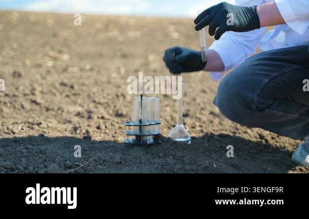 Agronomist in a lab coat and gloves taking soil samples with ...