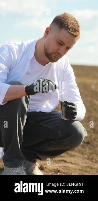 Agronomist in a white lab coat and black gloves collecting soil samples ...
