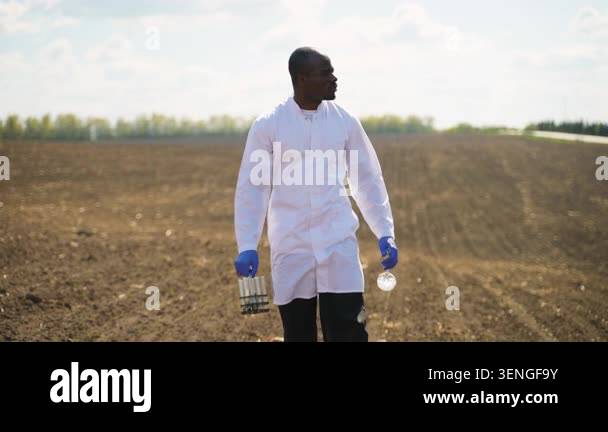 Agronomist wearing a lab coat and gloves walks through a plowed field ...