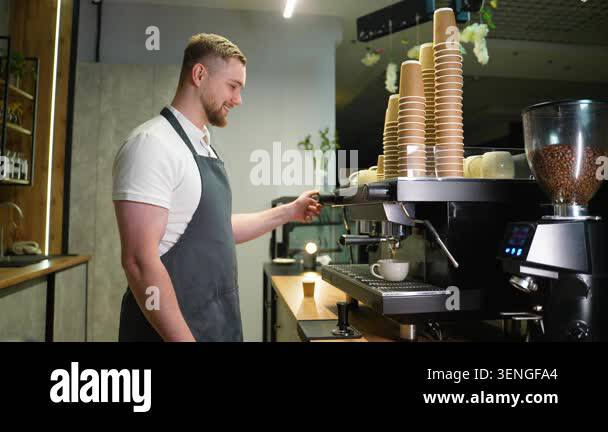 Young smiling male barista preparing a fresh cup of espresso using a ...