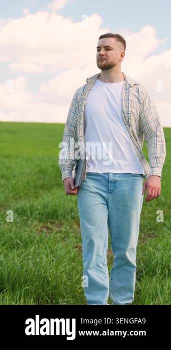 Modern agronomist walking through a lush green field, holding a laptop ...