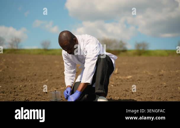 Male scientist in a lab coat and protective gloves gathering soil ...
