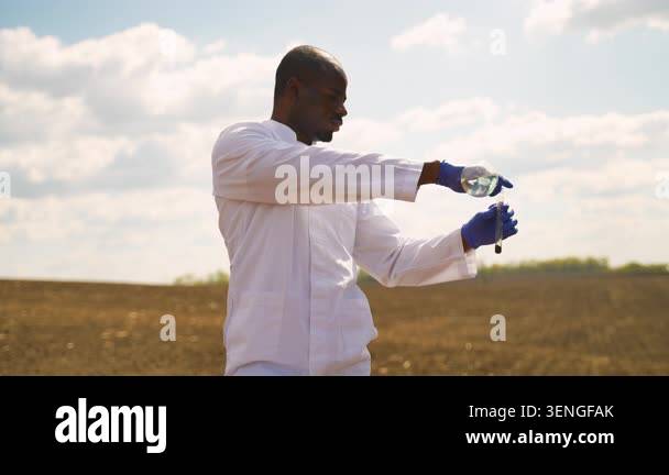 Laboratory worker in a white coat and gloves pouring a solution into a ...