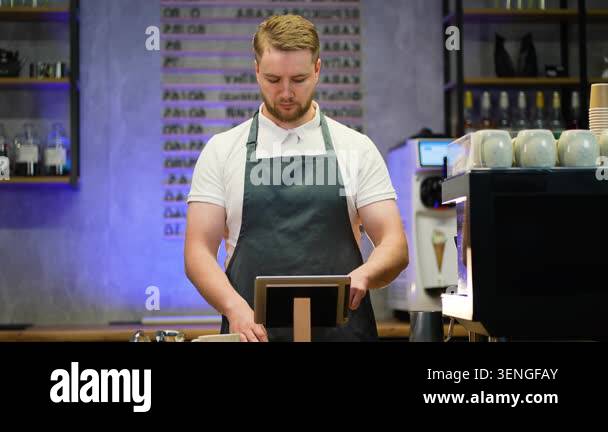Male worker in an apron using a modern digital tablet to take an order ...