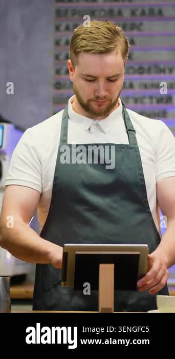 Young male bartender wearing an apron and working on a digital tablet ...