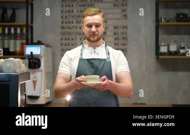 Friendly male barista in an apron holding a cup of freshly brewed ...