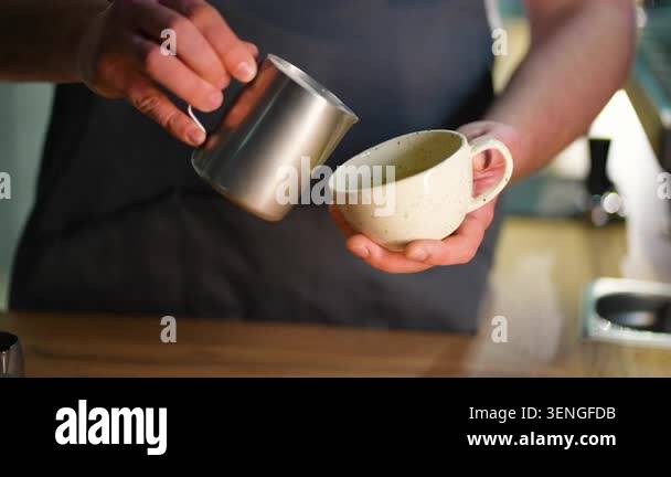 Close up of male barista hands pouring steamed milk into a coffee cup ...