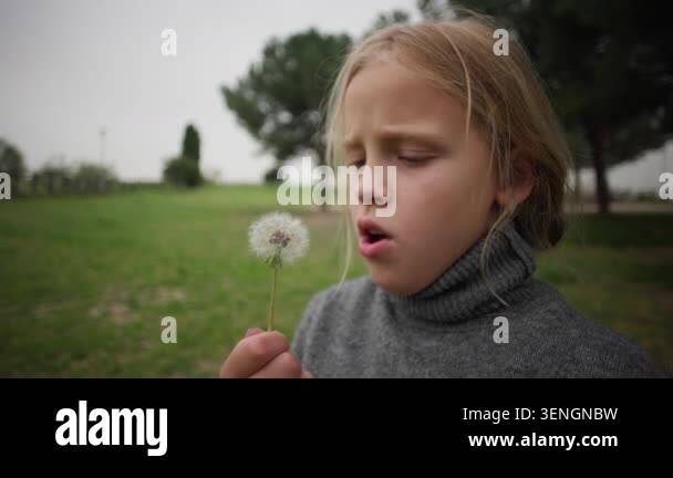 Close up profile of a blonde child puckering lips and blowing a fluffy ...