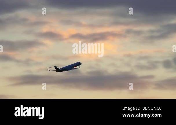Silhouette of a small regional jet climbing through pastel clouds at ...