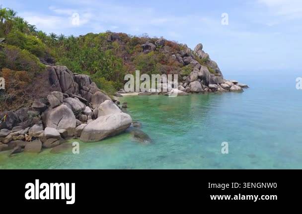 Aerial view flying over a rocky tropical bay with clear turquoise water ...