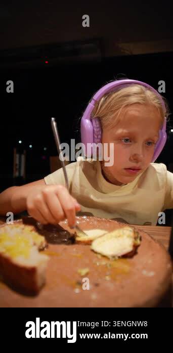 Young girl wearing purple headphones eats a meal at a cafe table in the ...
