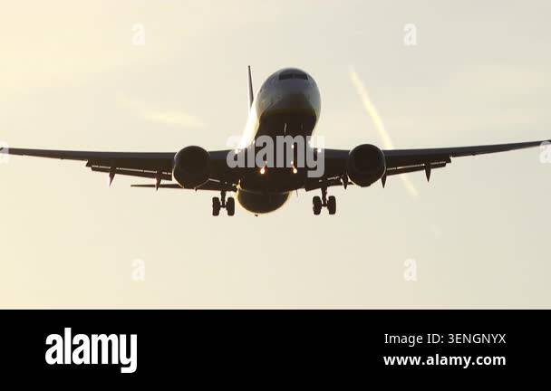 Twin engine airliner viewed head on during landing approach, backlit by ...