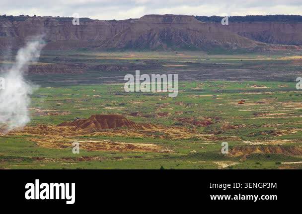 Tall column of white smoke rises above an arid badlands plain used as a ...