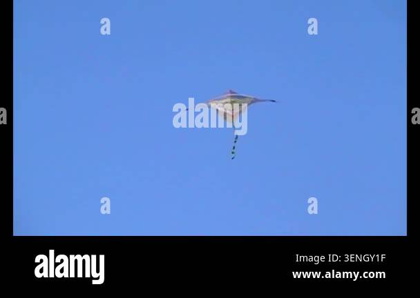 A colourful kite with a long tail floats high against a deep clear blue ...