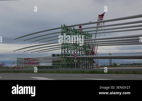 A tall lattice crane towers over rows of long white wind turbine blades ...