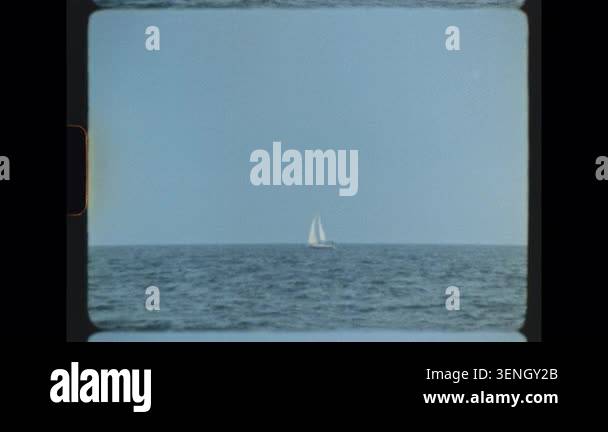 A single white sailboat glides far out on a calm blue sea beneath a ...