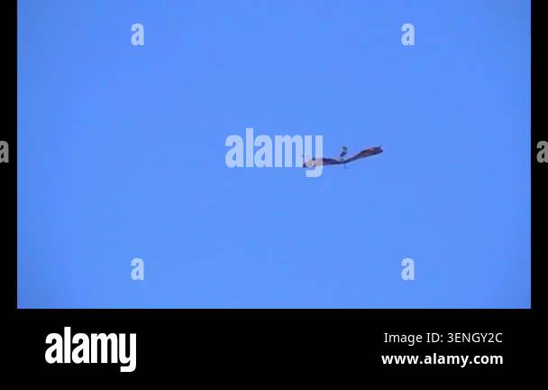 A slender colourful kite glides sideways high in a clear blue summer ...