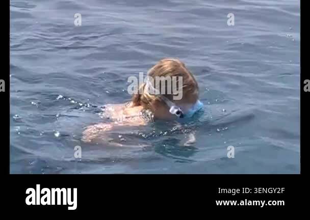 A young child swims with goggles head dipping toward the surface ...