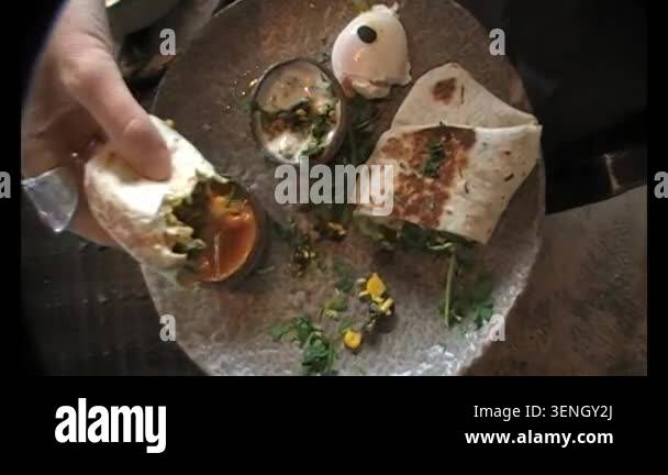 A hand holds a halved stuffed wrap above a rustic plate arranged with ...