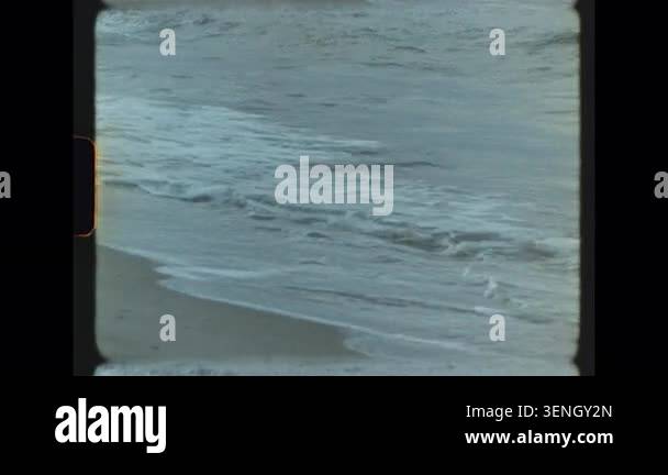 Soft foamy waves rolling onto a quiet sandy shore at dusk in muted blue ...