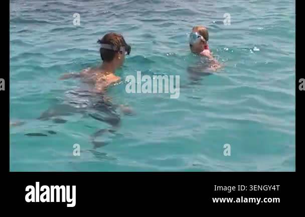Two children swim and snorkel side by side through clear turquoise ...