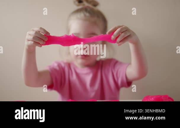 A young child stretches and molds bright pink slime while sitting at a ...