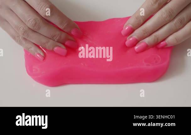 Two hands stretch and knead a pink slime on a flat surface. The light ...
