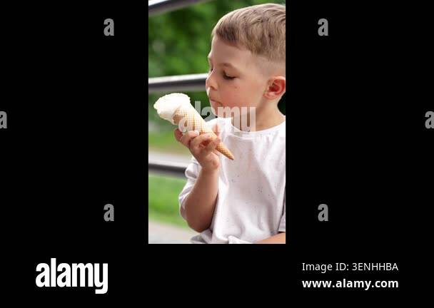 Happy blond boy with blue eyes eating ice cream cone outdoors on a ...