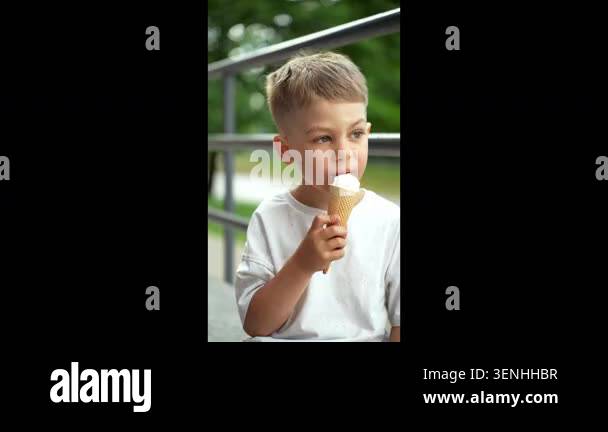 Happy blond boy with blue eyes eating ice cream cone outdoors on a ...
