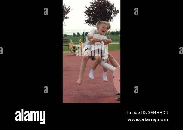 Vertical footage of two children laughing on a seesaw, showing joyful ...