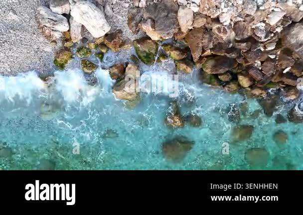 Aerial view of rocky shoreline with clear turquoise water gently ...