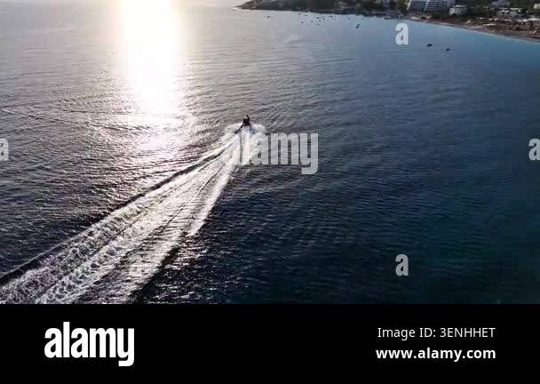 Motorboat glides across calm water, leaving a wake behind, with sun ...