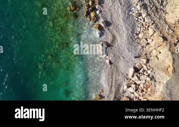 Aerial view of turquoise sea waves gently splashing against pebbles and ...