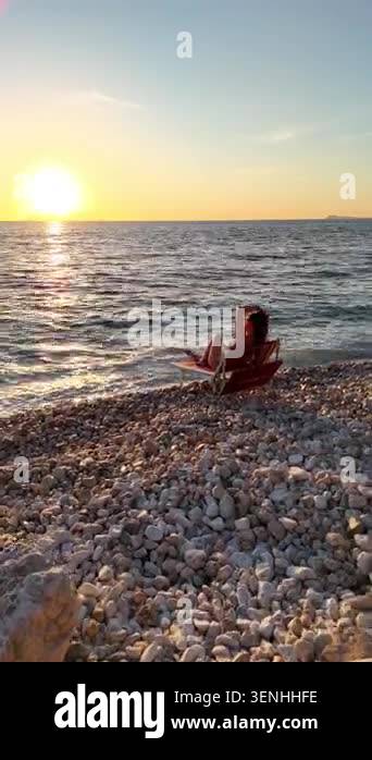 Young woman relaxes on a sun lounger by the sea at sunset. Girl ...