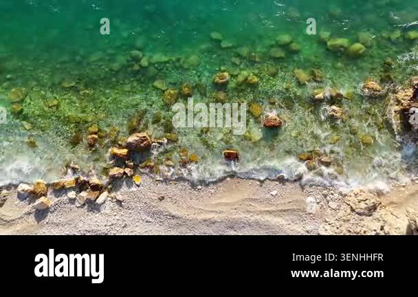 Aerial view of turquoise sea waves gently splashing against pebbles and ...