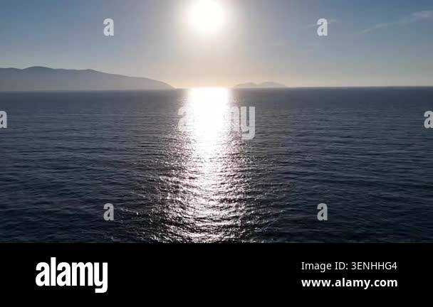 Aerial view of sun reflecting on calm sea waters with distant mountains ...