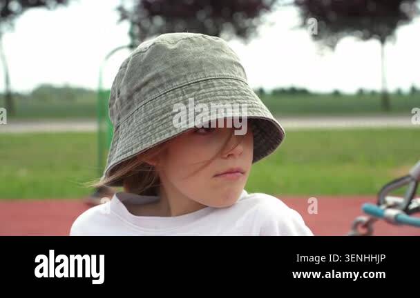 Child sitting on playground wearing a panama hat, expressing refusal or ...