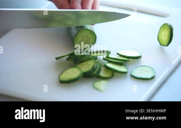 Close-up of a woman's hands slicing a fresh green cucumber with a chef ...
