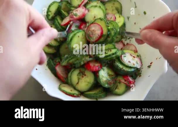 Close-up of preparing a simple summer salad by tossing sliced cucumbers ...