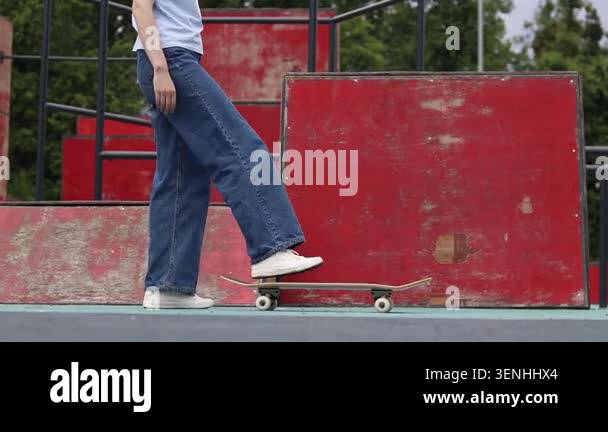 Girl in wide jeans getting ready to skateboard in skate park. Skater ...