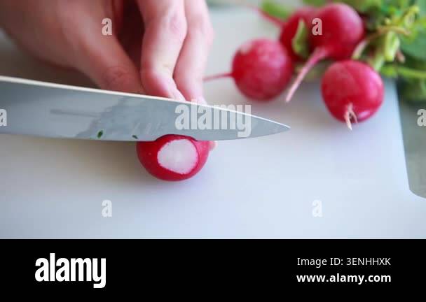 Close-up of a woman's hands slicing fresh red radishes with a chef's ...