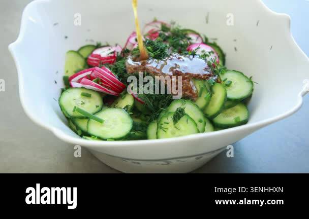 Close-up of preparing a simple summer salad by tossing sliced cucumbers ...