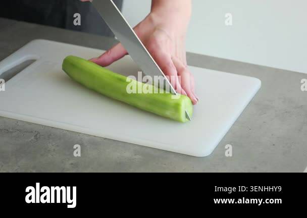 Close-up of a woman's hands slicing a fresh green cucumber with a chef ...