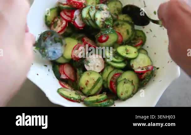 Close-up of preparing a simple summer salad by tossing sliced cucumbers ...