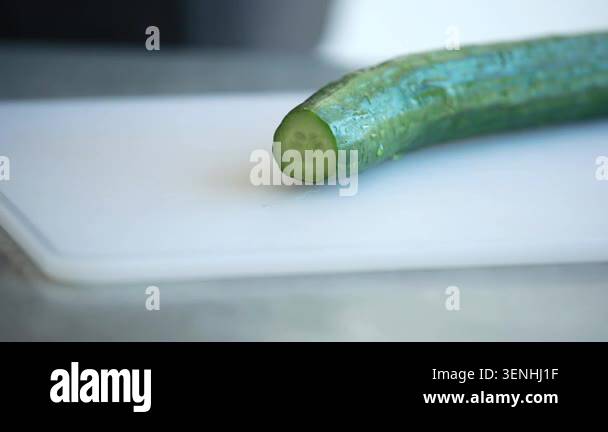 Close-up of a woman's hands slicing a fresh green cucumber with a chef ...
