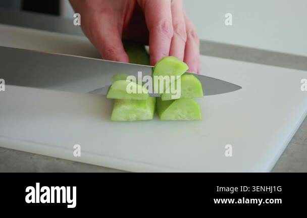 Close-up of a woman's hands slicing a fresh green cucumber with a chef ...